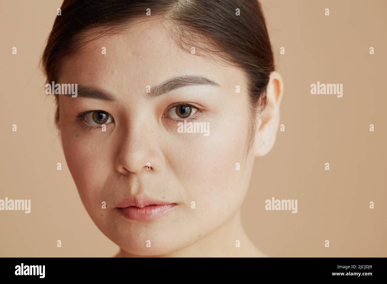 Portrait of modern asian woman looking in camera on beige background ...