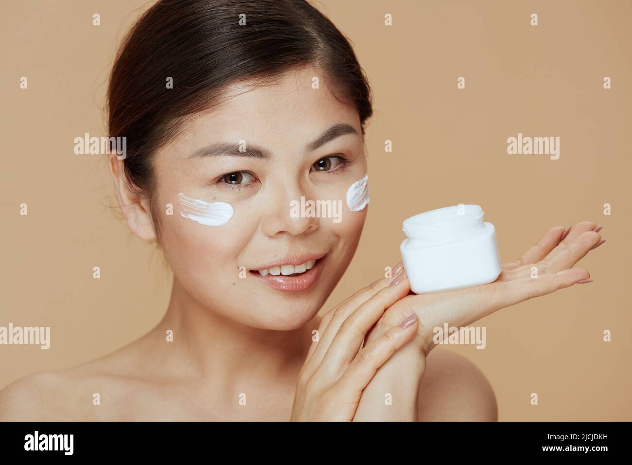Portrait of modern asian female with facial cream jar and facial cream ...