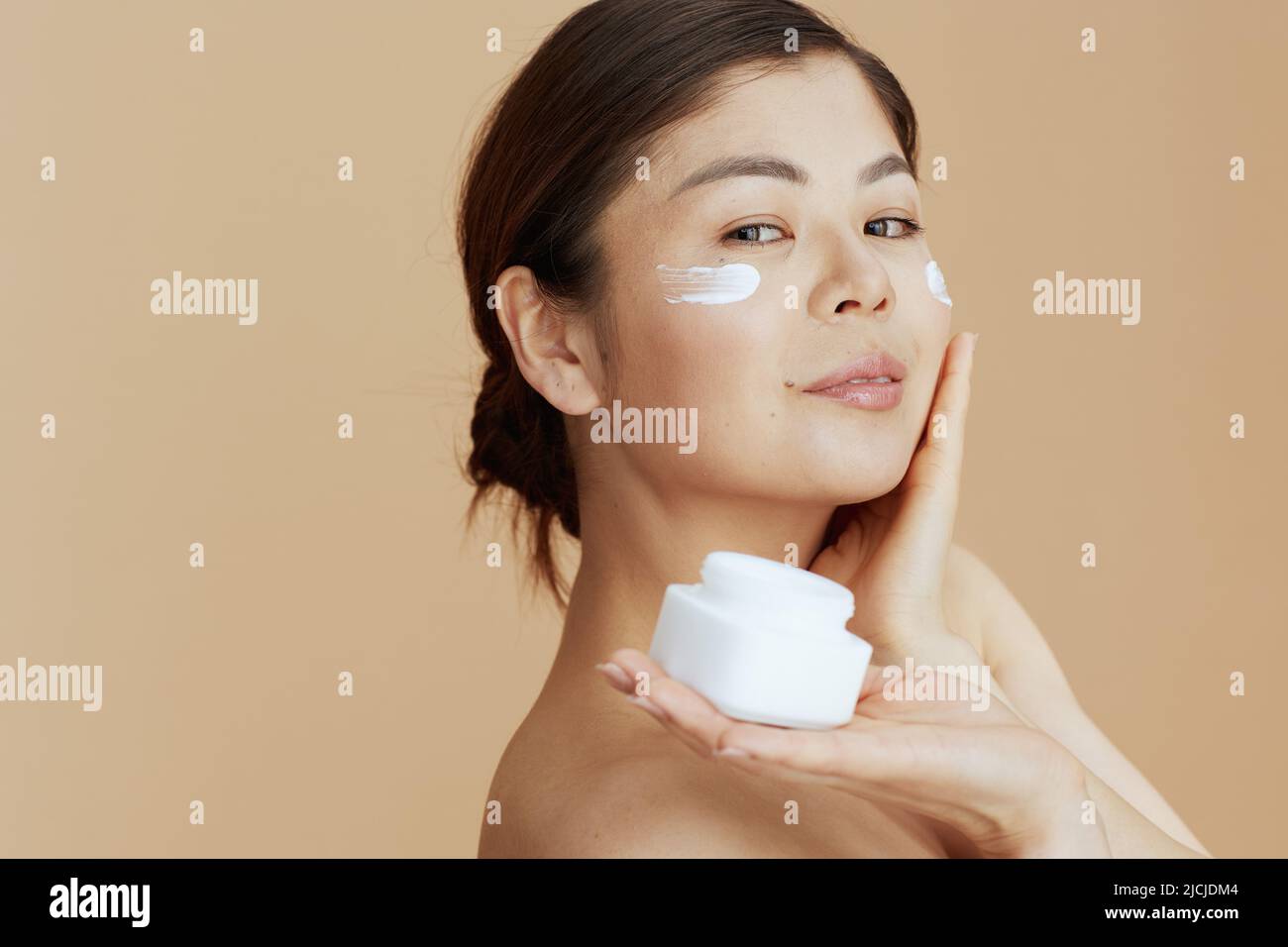 modern woman with facial cream jar and facial cream on face on beige background Stock Photo - Alamy