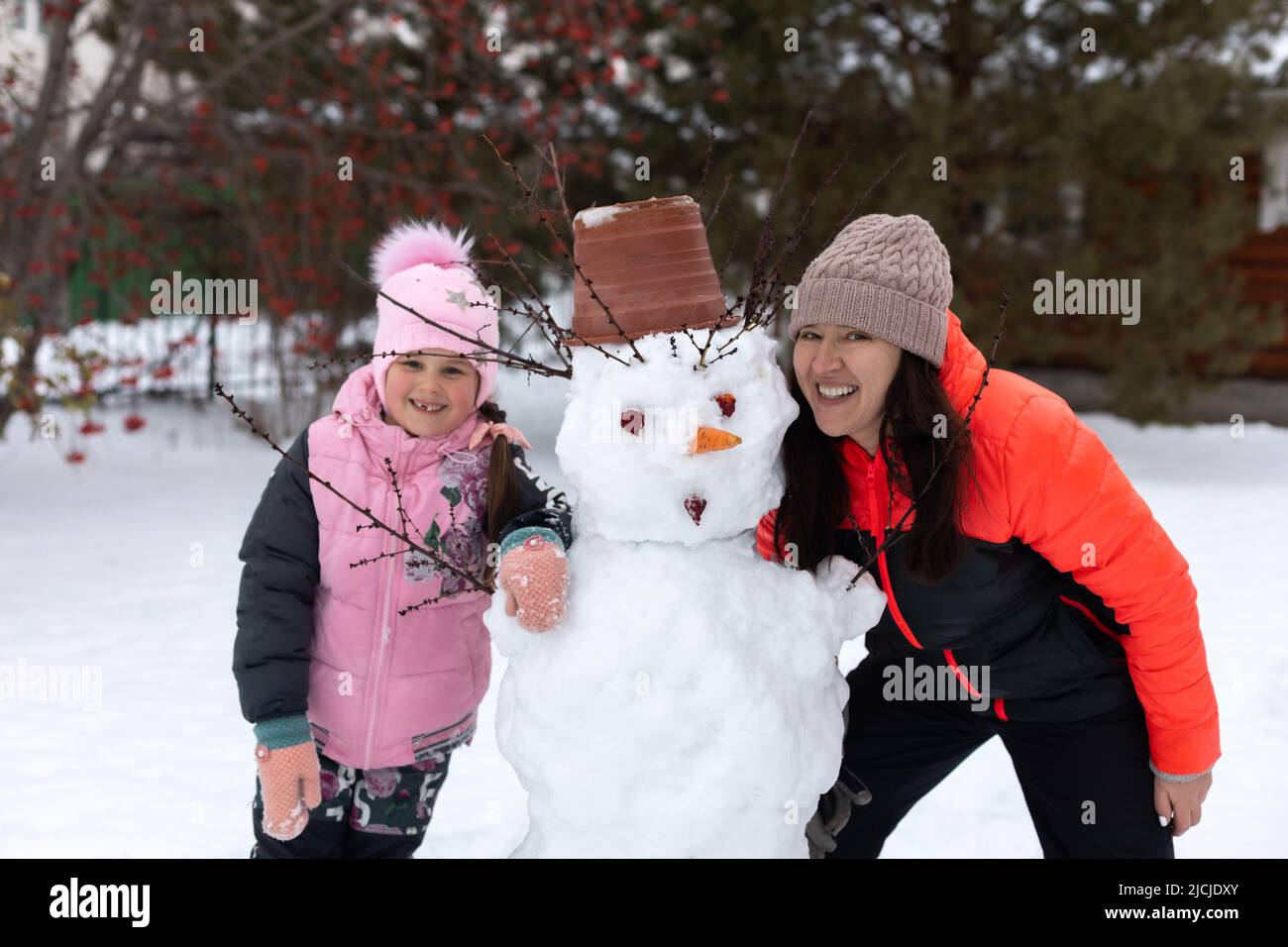 Portrait of little girl and woman with built snowman with snow smiling ...