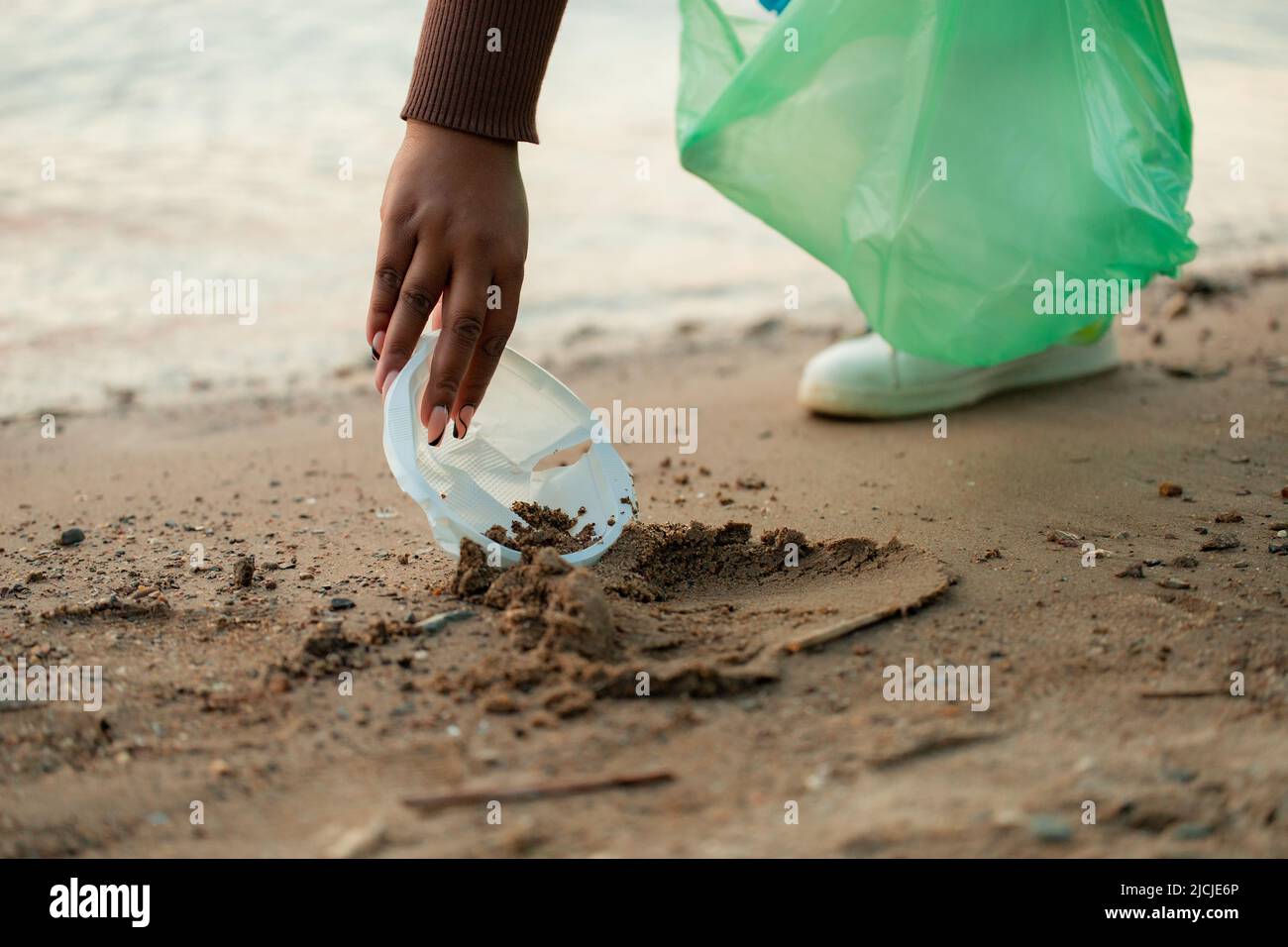 Cropped photo of African woman collecting spilled garbage from sand on ...