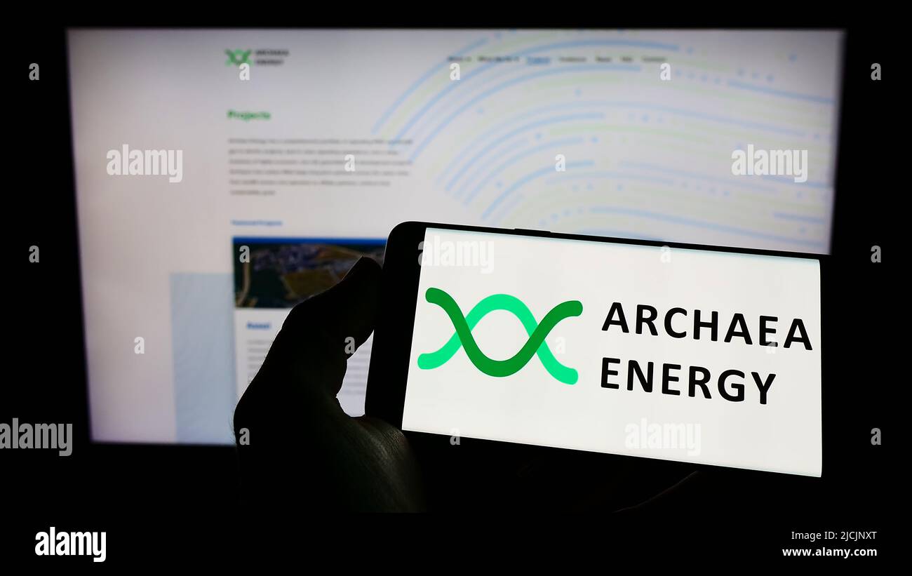 Person holding cellphone with logo of US gas company Archaea Energy Inc. on screen in front of ...