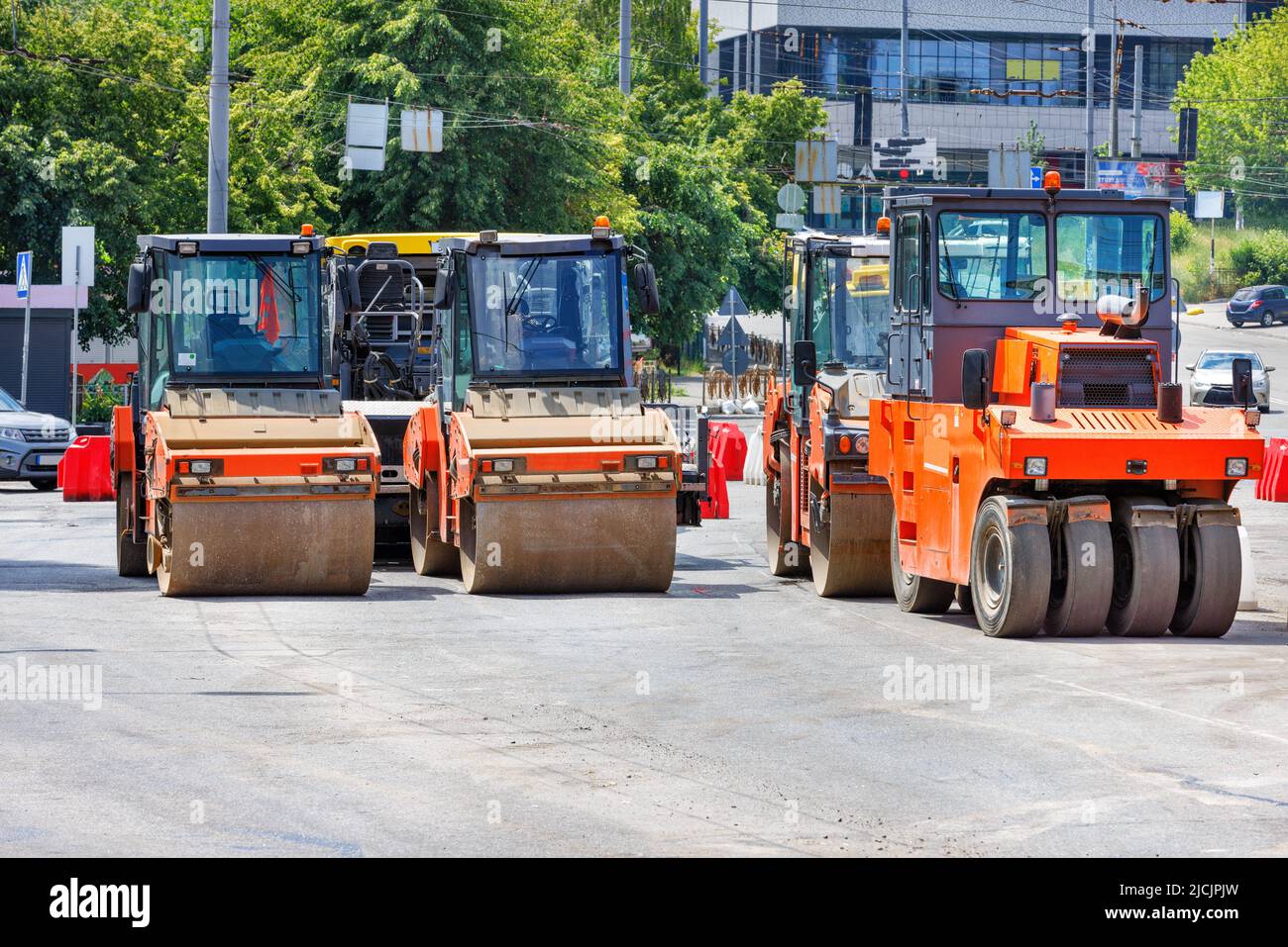 Orange industrial road rollers line up on a city street on a sunny day ...