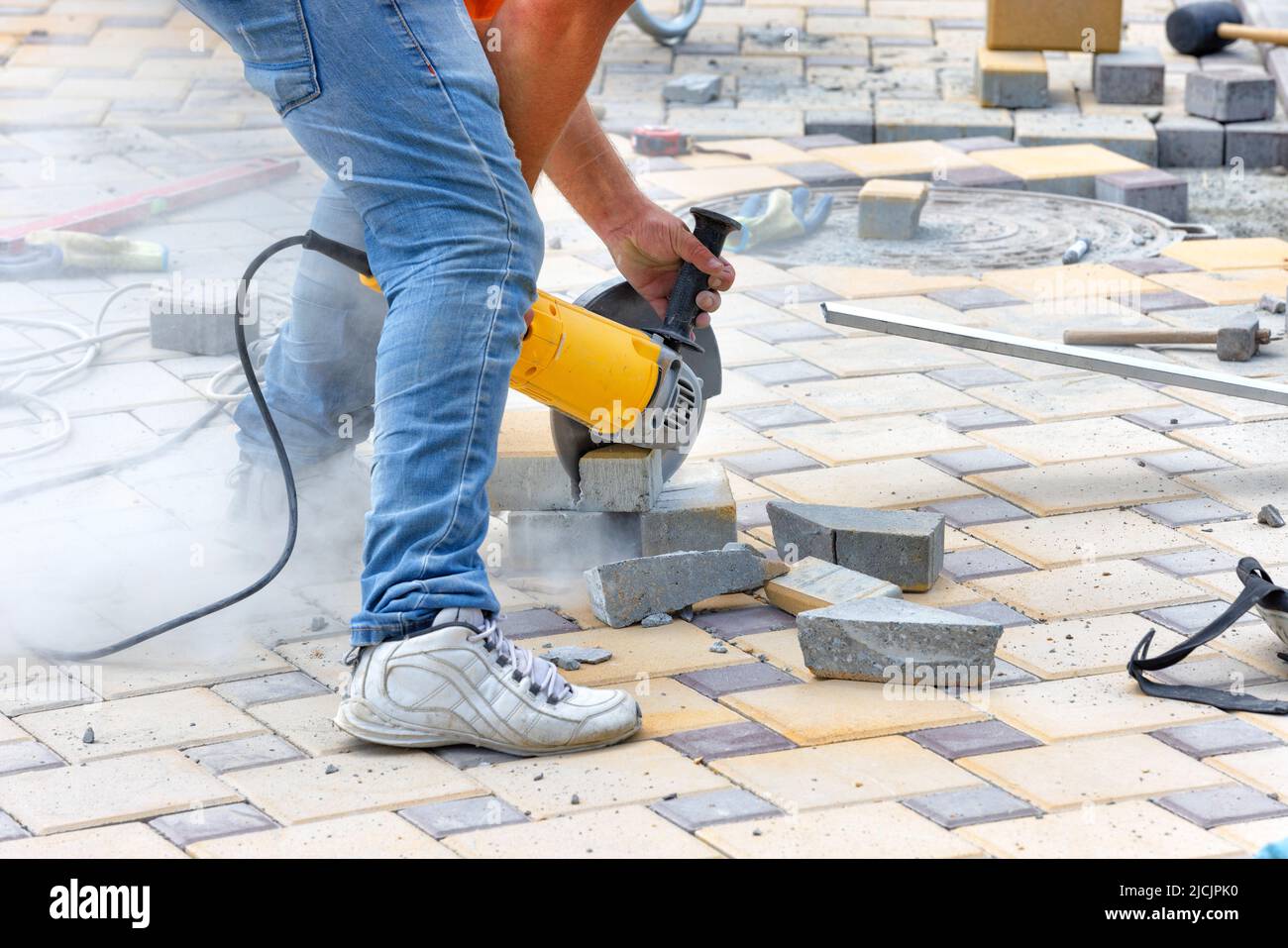 A worker using an electric cutter and a cutting disc cuts paving slabs ...