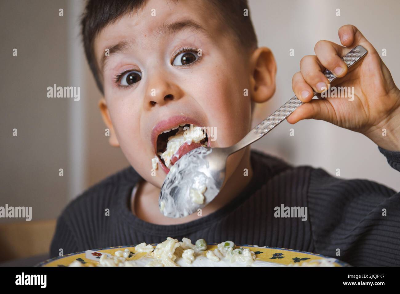 Portrait of small caucasian boy sitting by the table at home eating ...