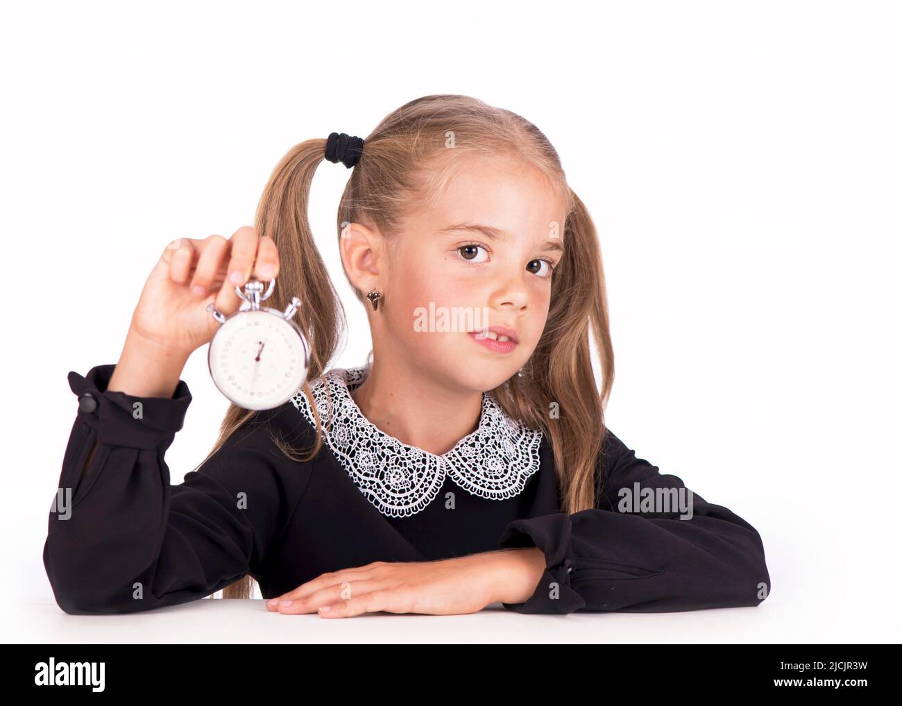 Little girl, blonde in a school dress points to a stopwatch on a white ...