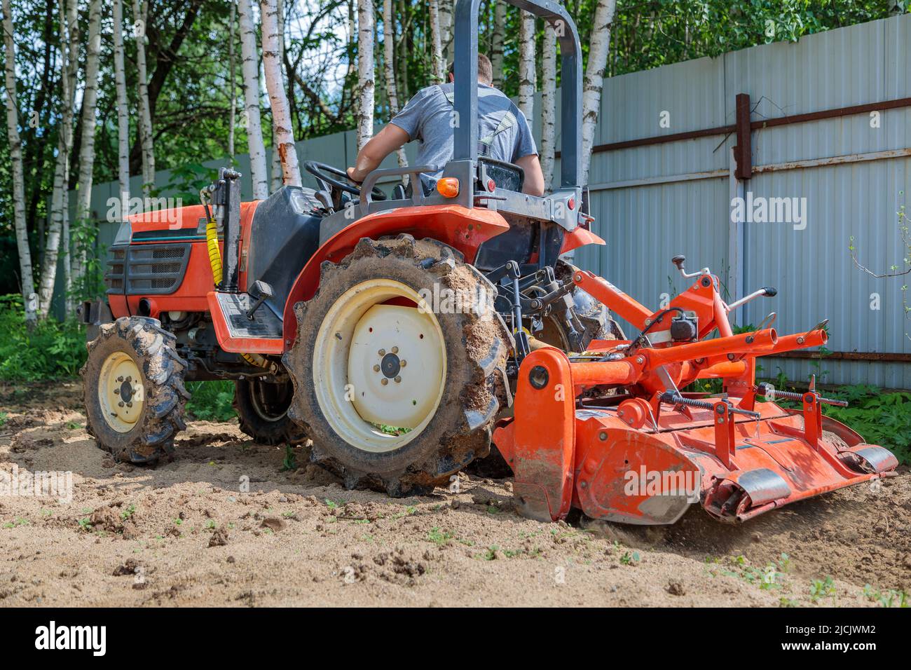 A farmer on a mini tractor loosens the soil for the lawn. Land ...