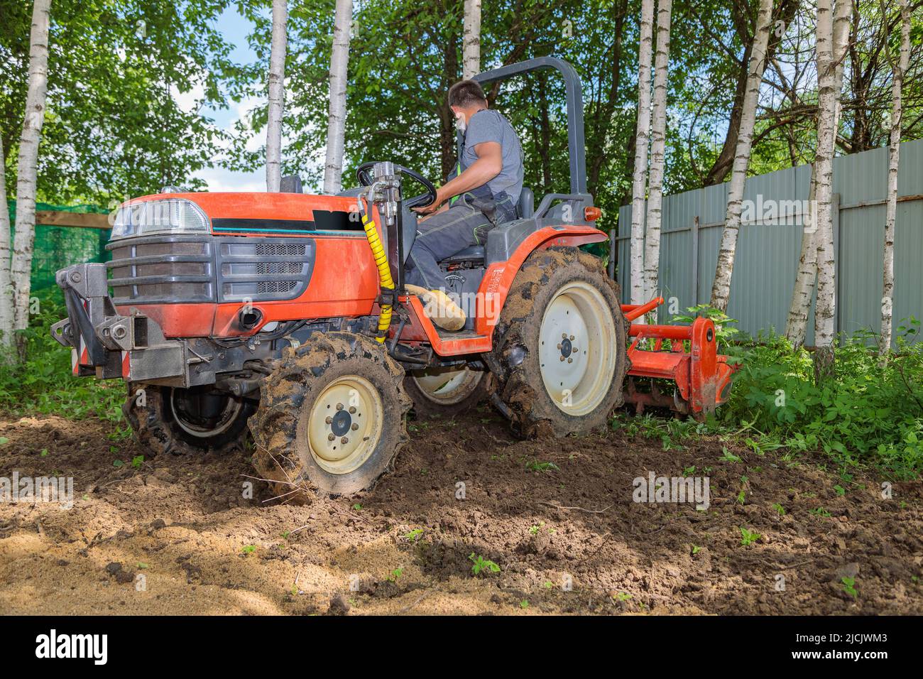 A farmer on a mini tractor loosens the soil for the lawn. Land ...