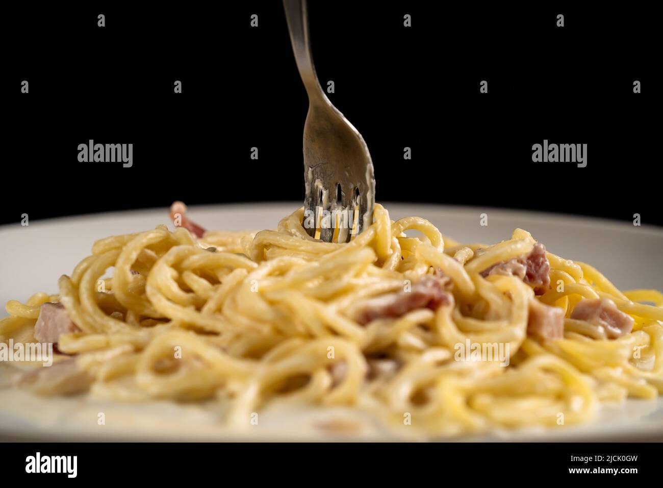 fork is spinning carbonara spaghetti on white plate on a black ...