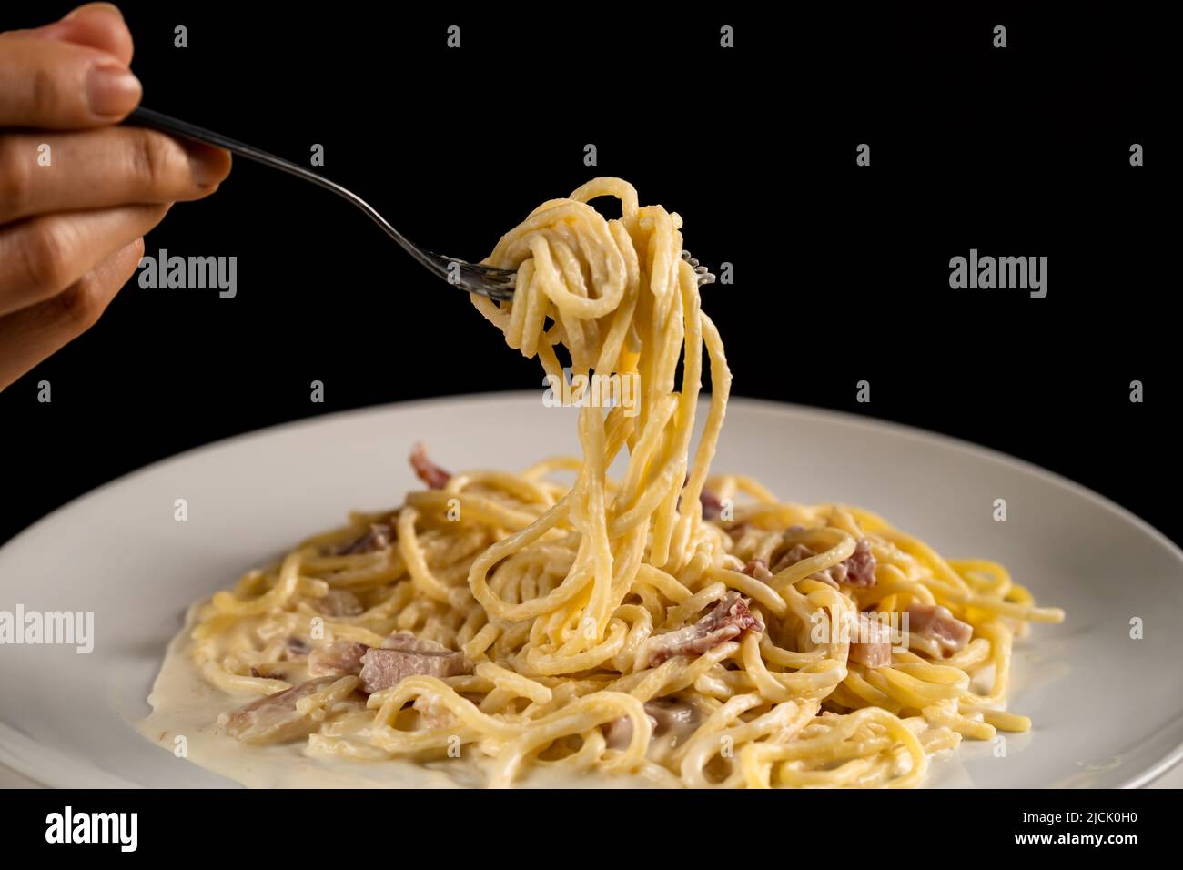 fork is spinning carbonara spaghetti on white plate on a black ...