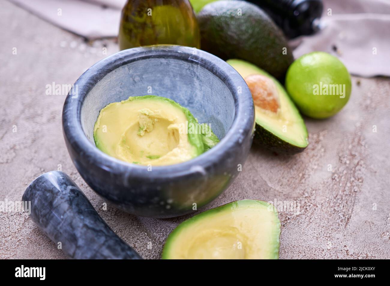 fresh avocado cut in half and marble mortar on grey concrete table ...