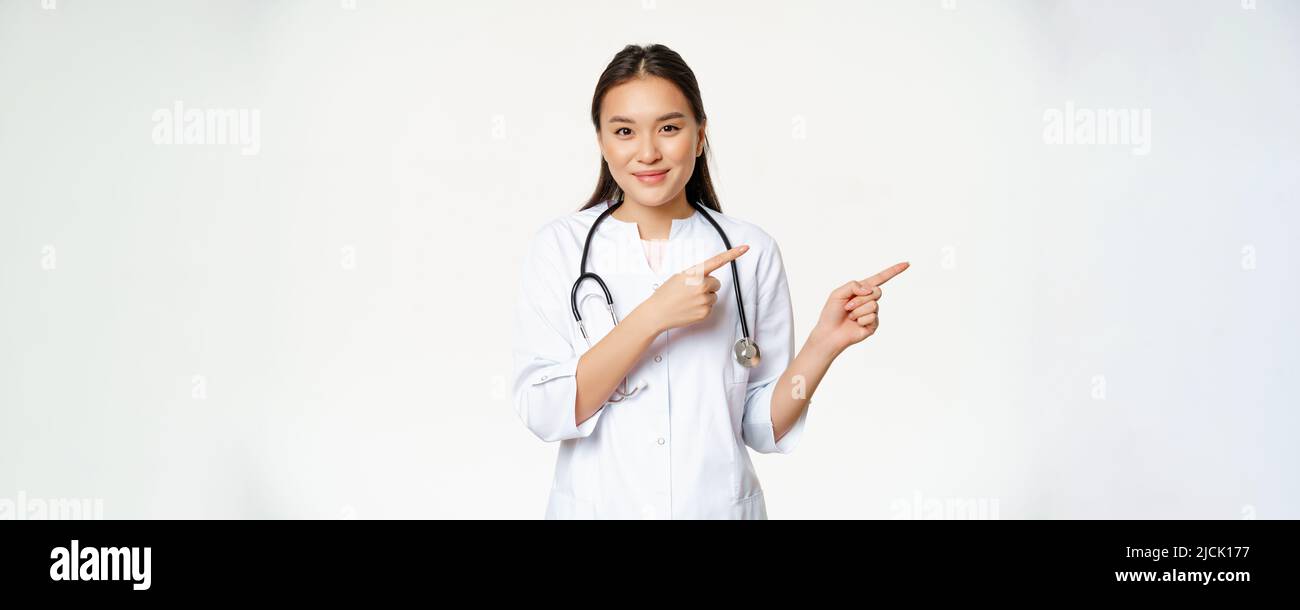 Healthcare, medical people concept. Smiling asian female doctor, pointing fingers right, showing ...