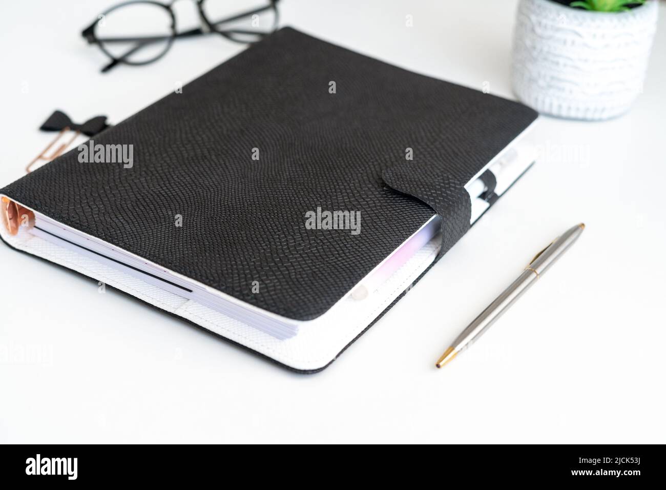 Close up picture of black notepad on white table with glasses, pen and ...
