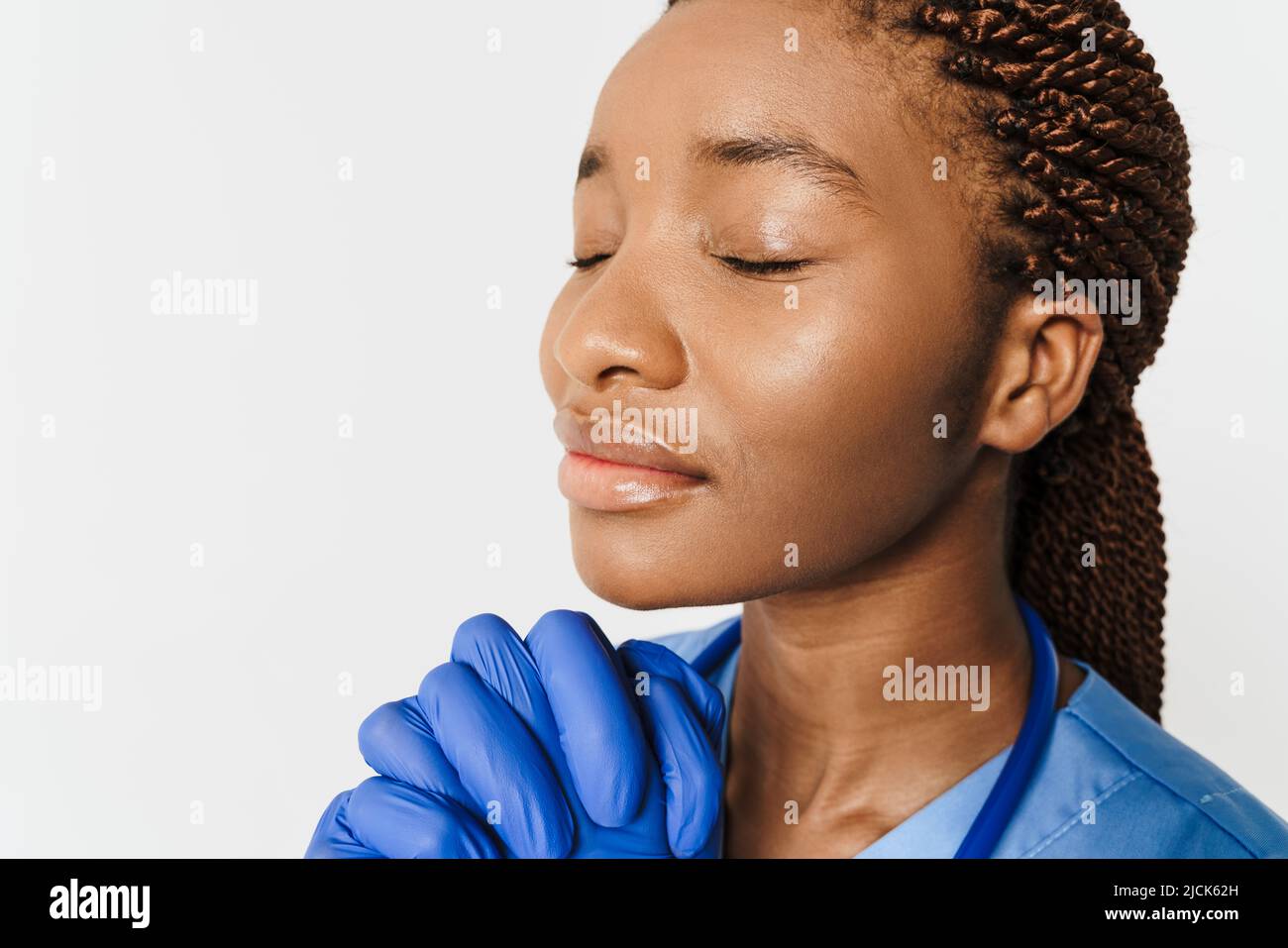 Young black doctor wearing uniform making prayer gesture isolated over ...