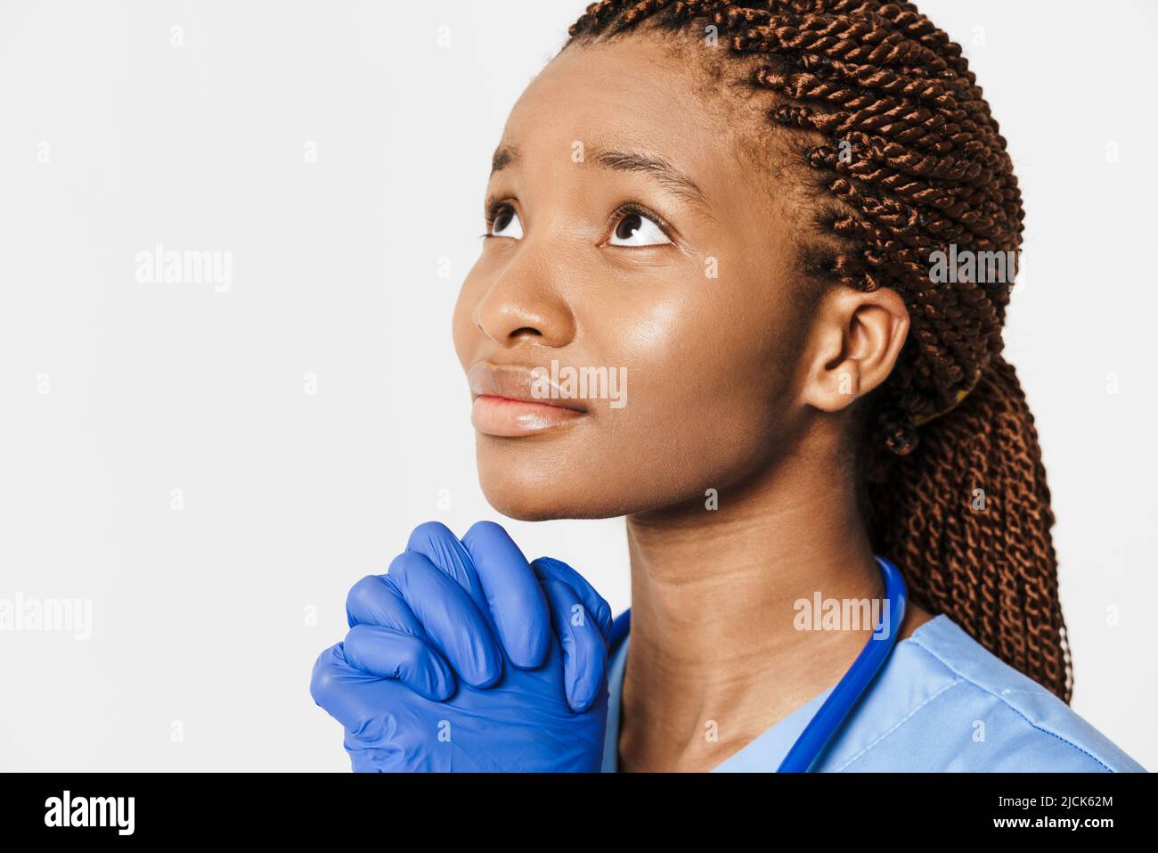 Young black doctor wearing uniform making prayer gesture isolated over ...
