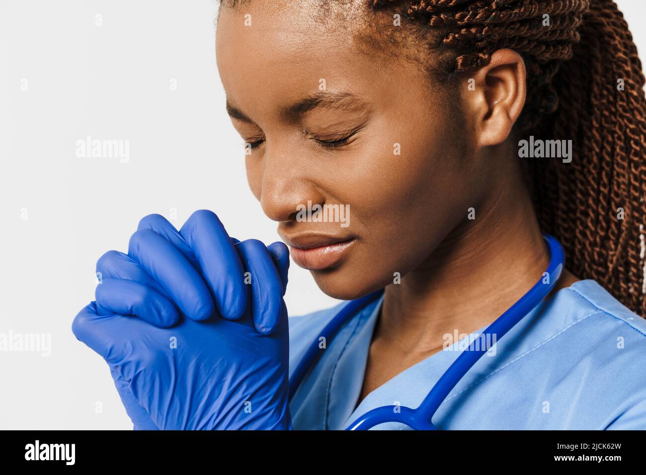 Young black doctor wearing uniform making prayer gesture isolated over ...