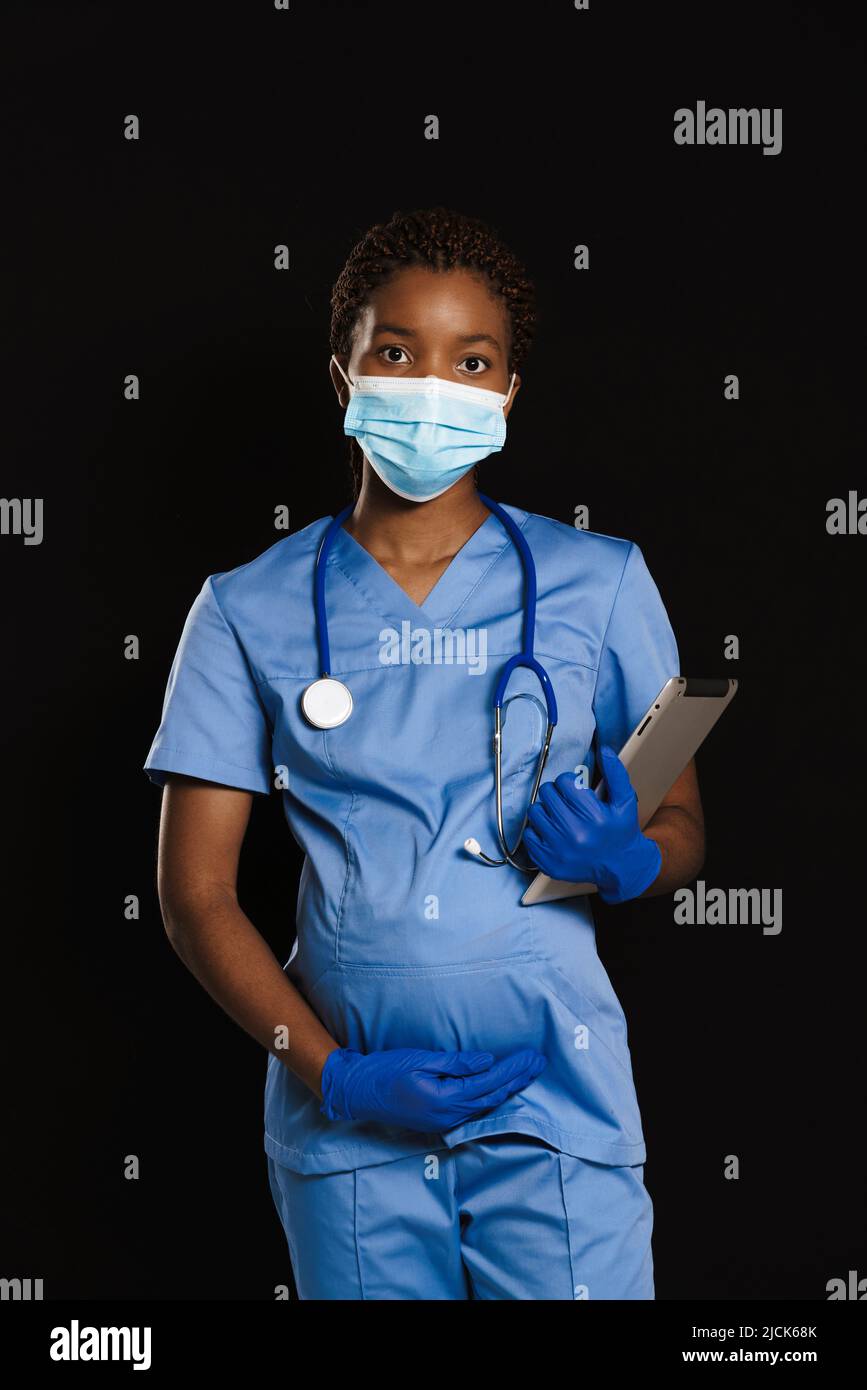 Black pregnant doctor in face mask posing with tablet computer isolated ...