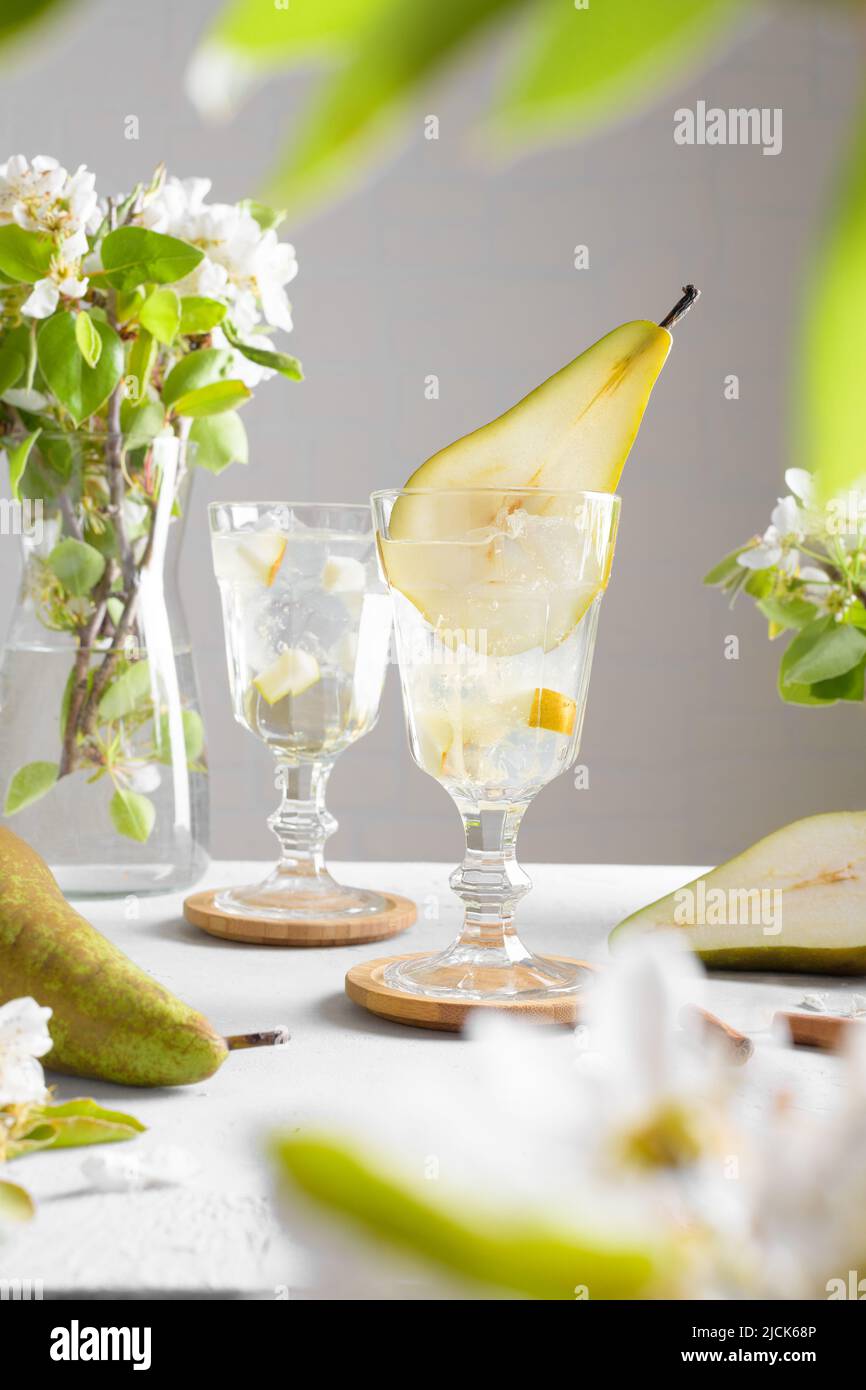 Pear cocktail with pear puree and fresh fruit and flowers on light gray ...