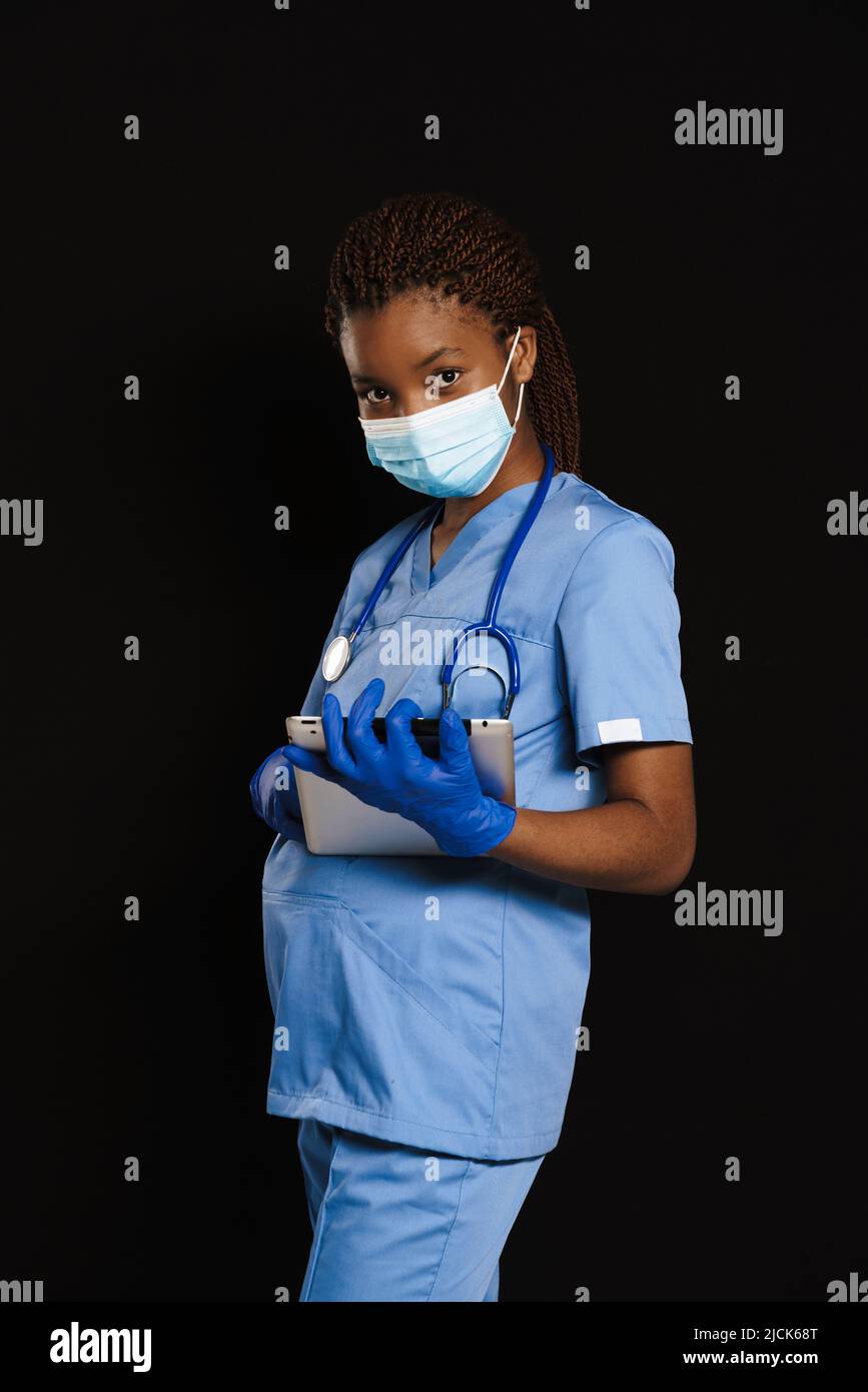 Black pregnant doctor in face mask posing with tablet computer isolated ...