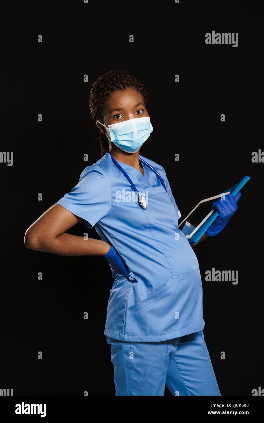 Black pregnant doctor in face mask posing with tablet computer isolated ...