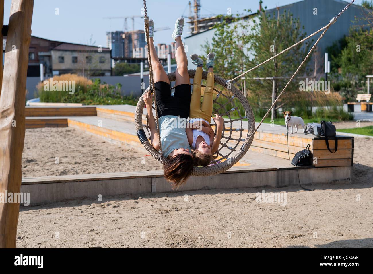 Mom and daughter swing on a round swing. Caucasian woman and little girl have fun on the ...