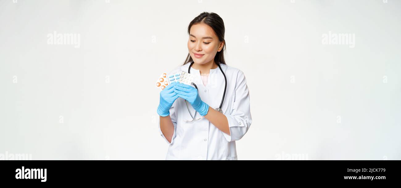 Smiling asian doctor showing medical pills, advertising vitamins ...