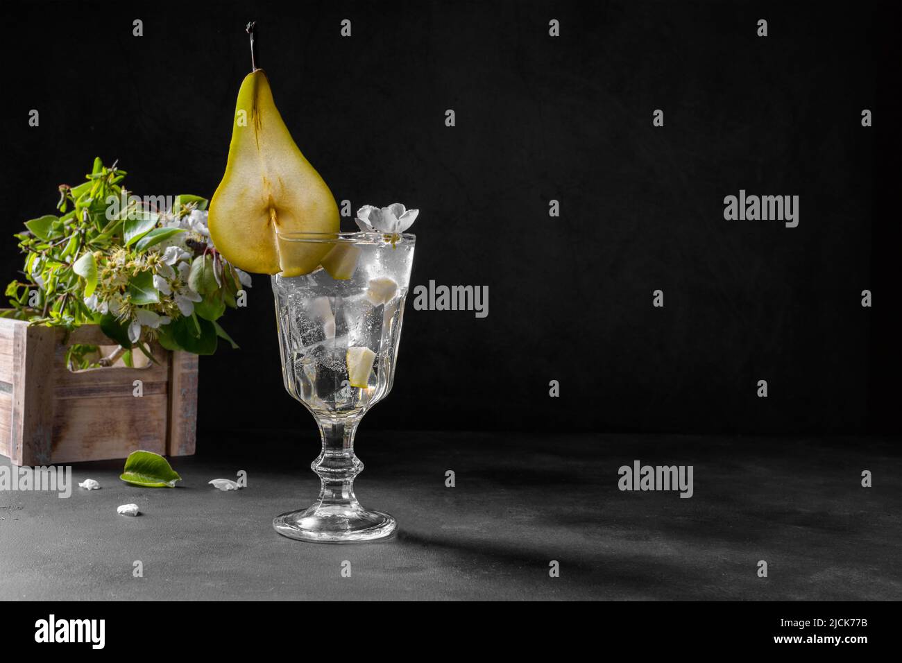 Pear cocktail in a glass decorated with fresh fruit and flowers on dark ...