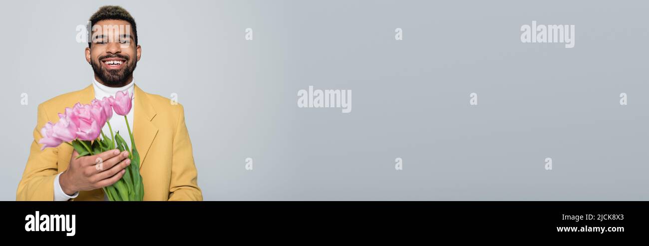 happy african american man in stylish outfit holding bouquet of pink ...