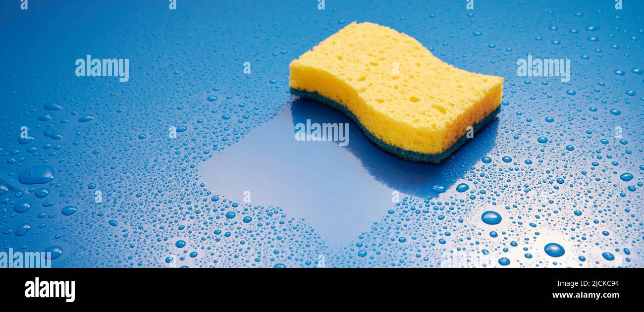 Yellow wash scrub sponge placed on wet blue background covered with ...