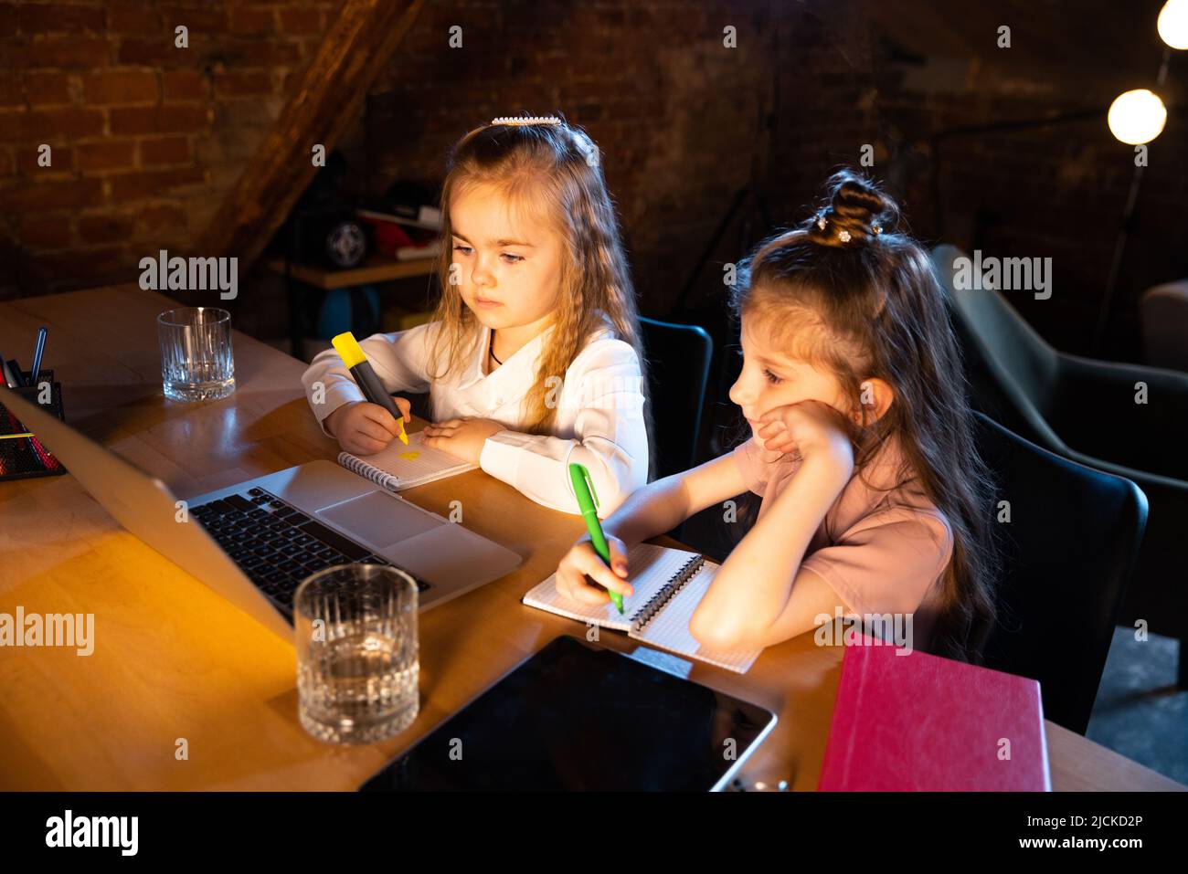 Live portrait of cute kids, sisters sitting at home play computer games ...