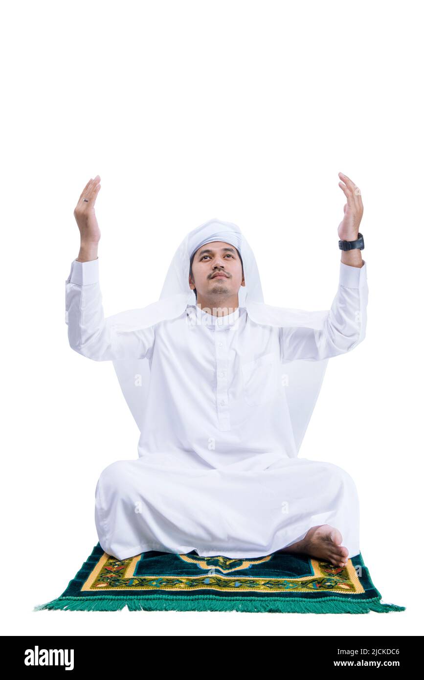 Muslim man praying while sitting on the prayer rug isolated over white ...