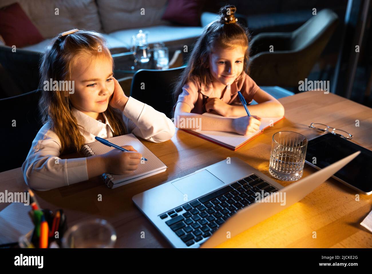 Two little cute kids, sisters sitting at home and doing homework at ...