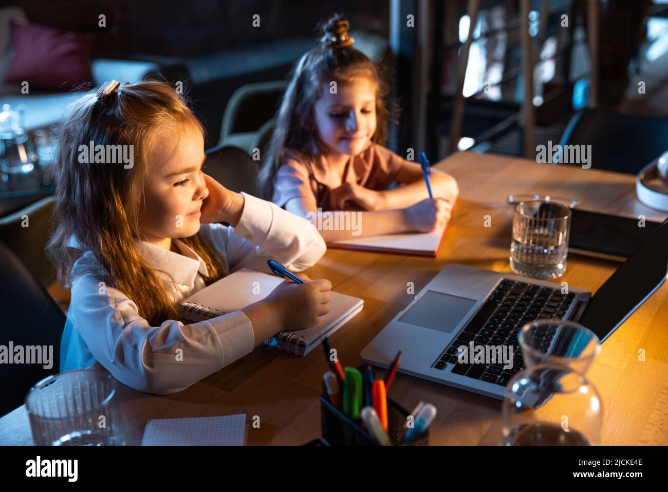 Live portrait of cute kids, sisters sitting at home play computer games ...