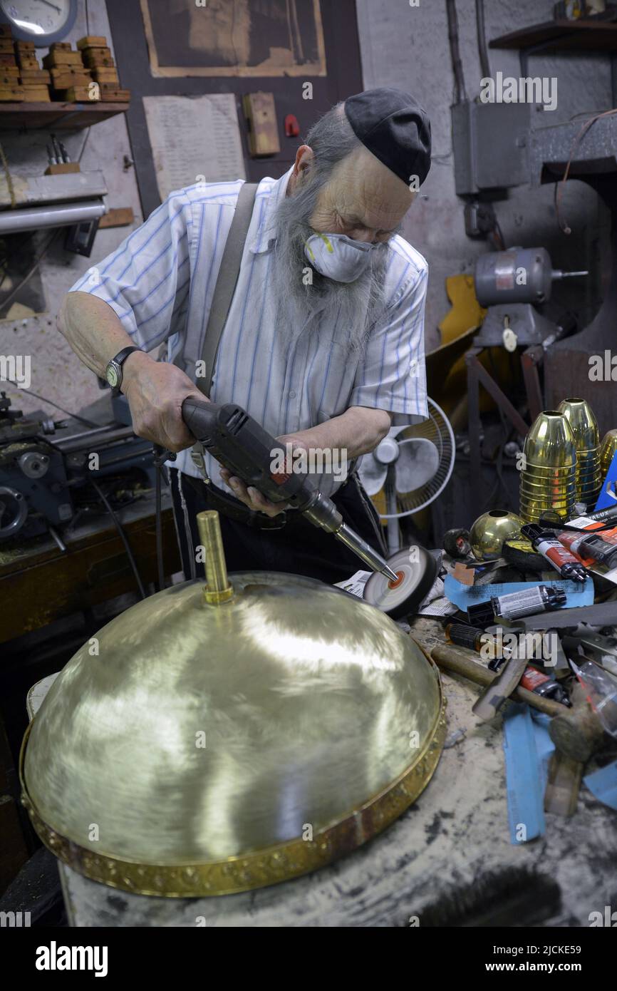 A Jewish silversmith and master craftsman works polishing the base of a ...