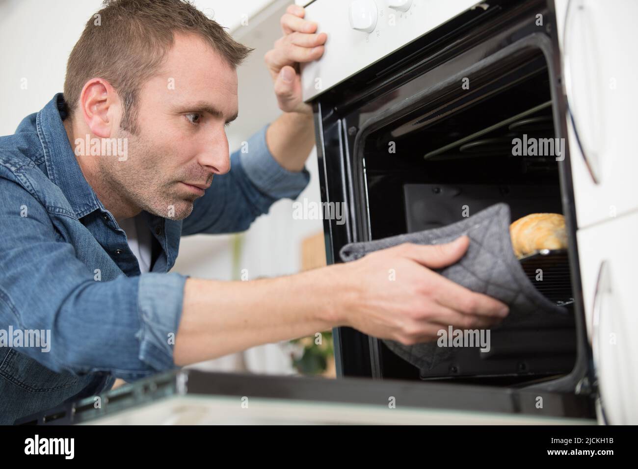 man taking baked loafs of bread out of the oven Stock Photo - Alamy