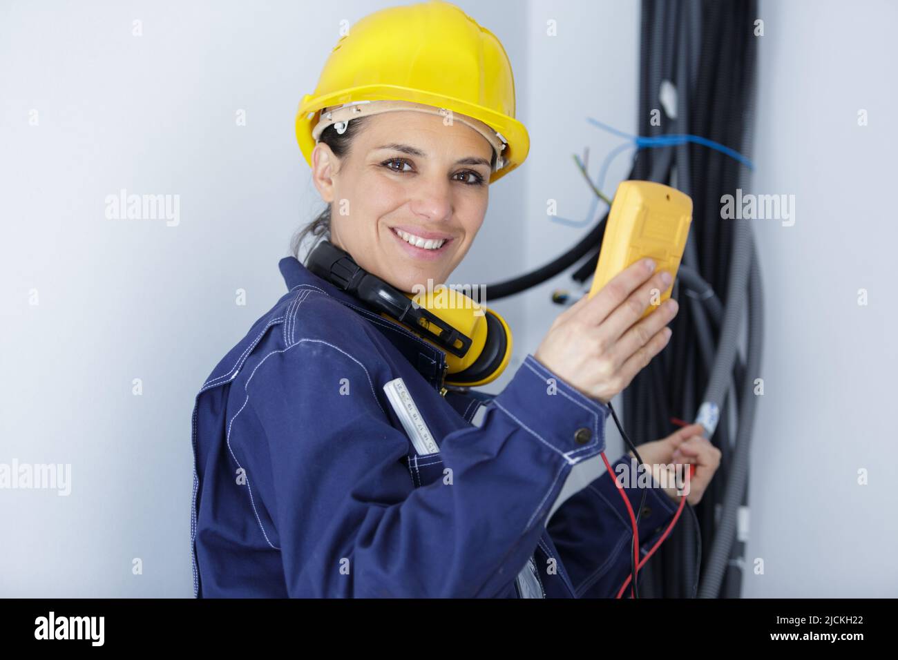 portrait of female builder checking wiring installation with multimeter ...