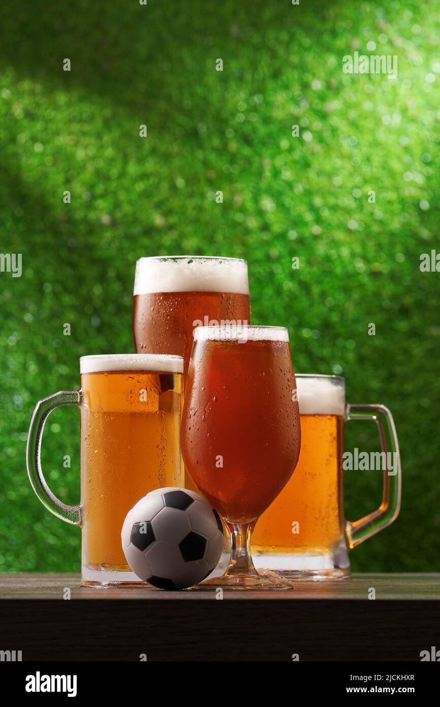 Four glasses of beer with soccer ball on the green grass background ...