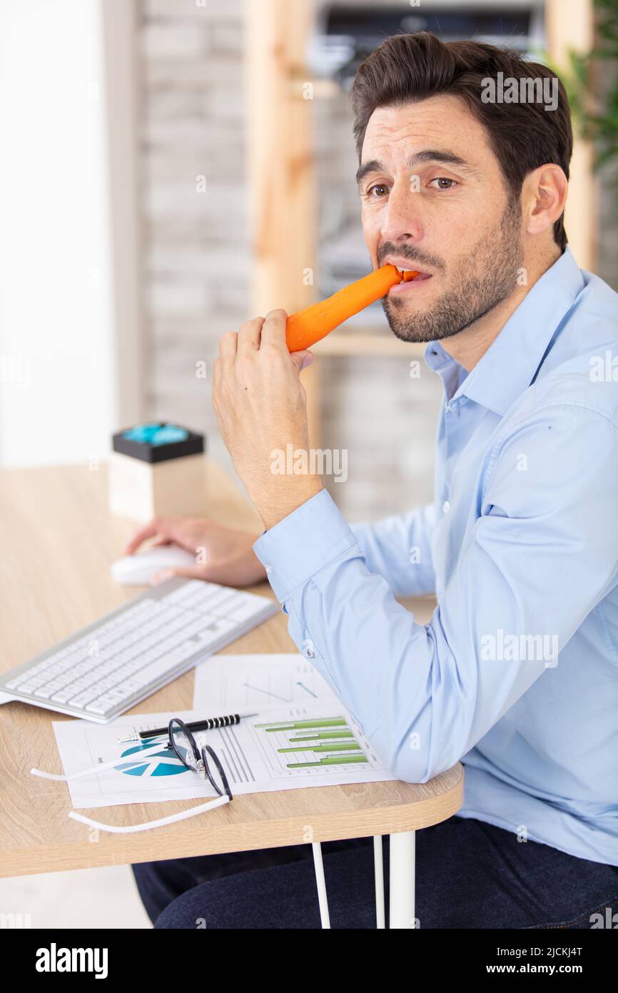 young man at computer desk eating raw carrot Stock Photo - Alamy