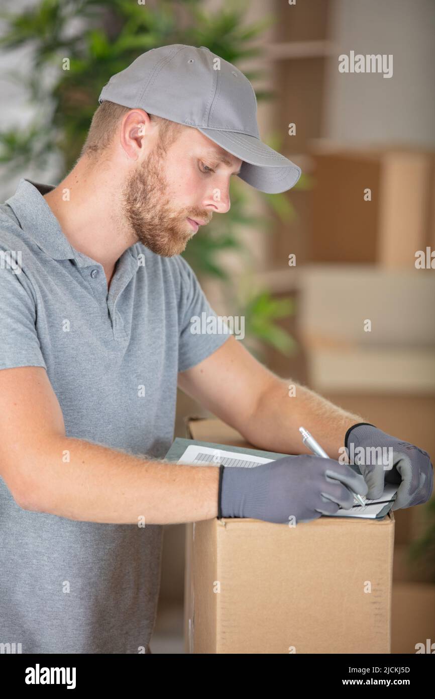 deliveryman leaning on cardboard box to fill in paperwork Stock Photo ...