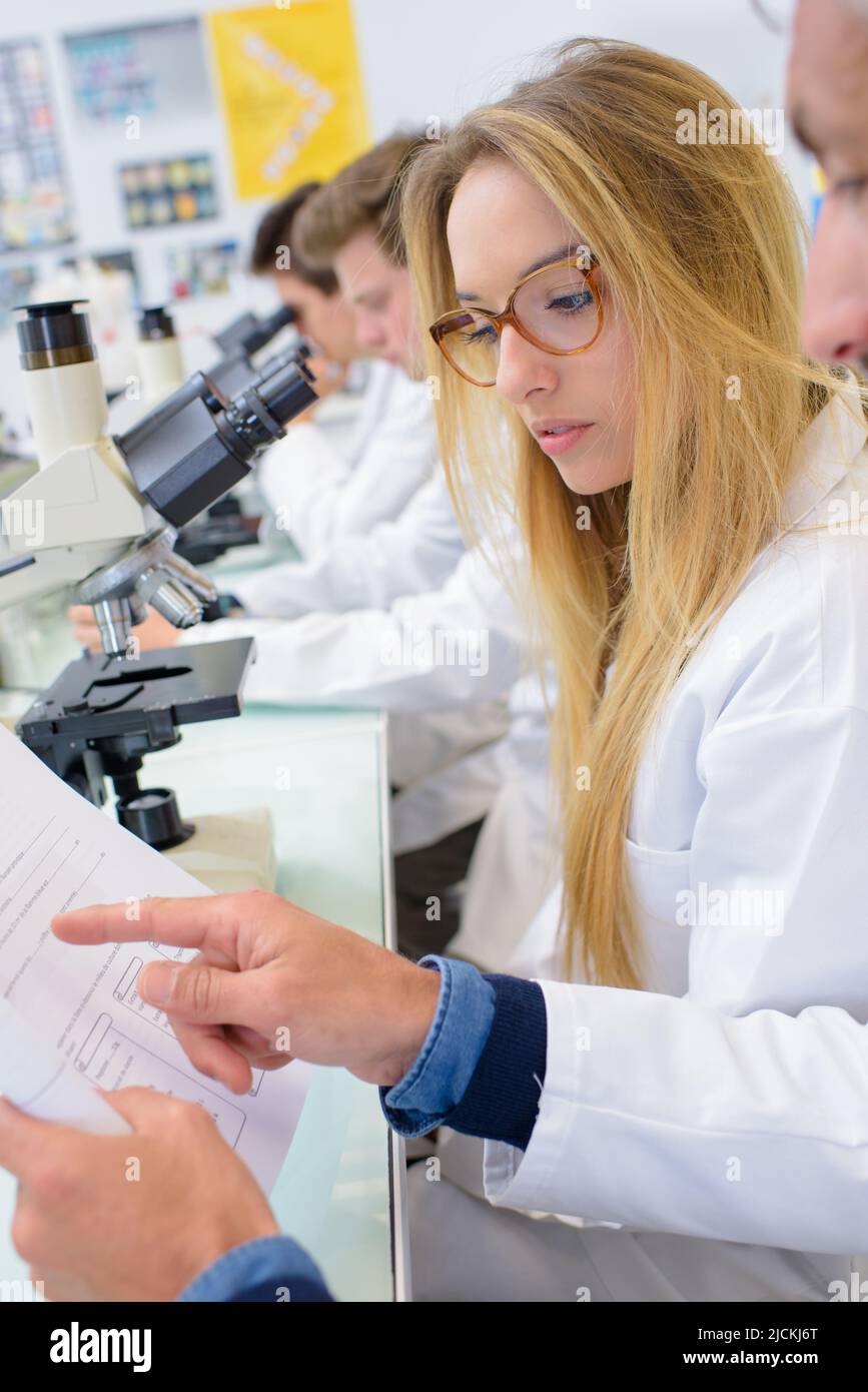 Teacher reading from paperwork to science student Stock Photo - Alamy