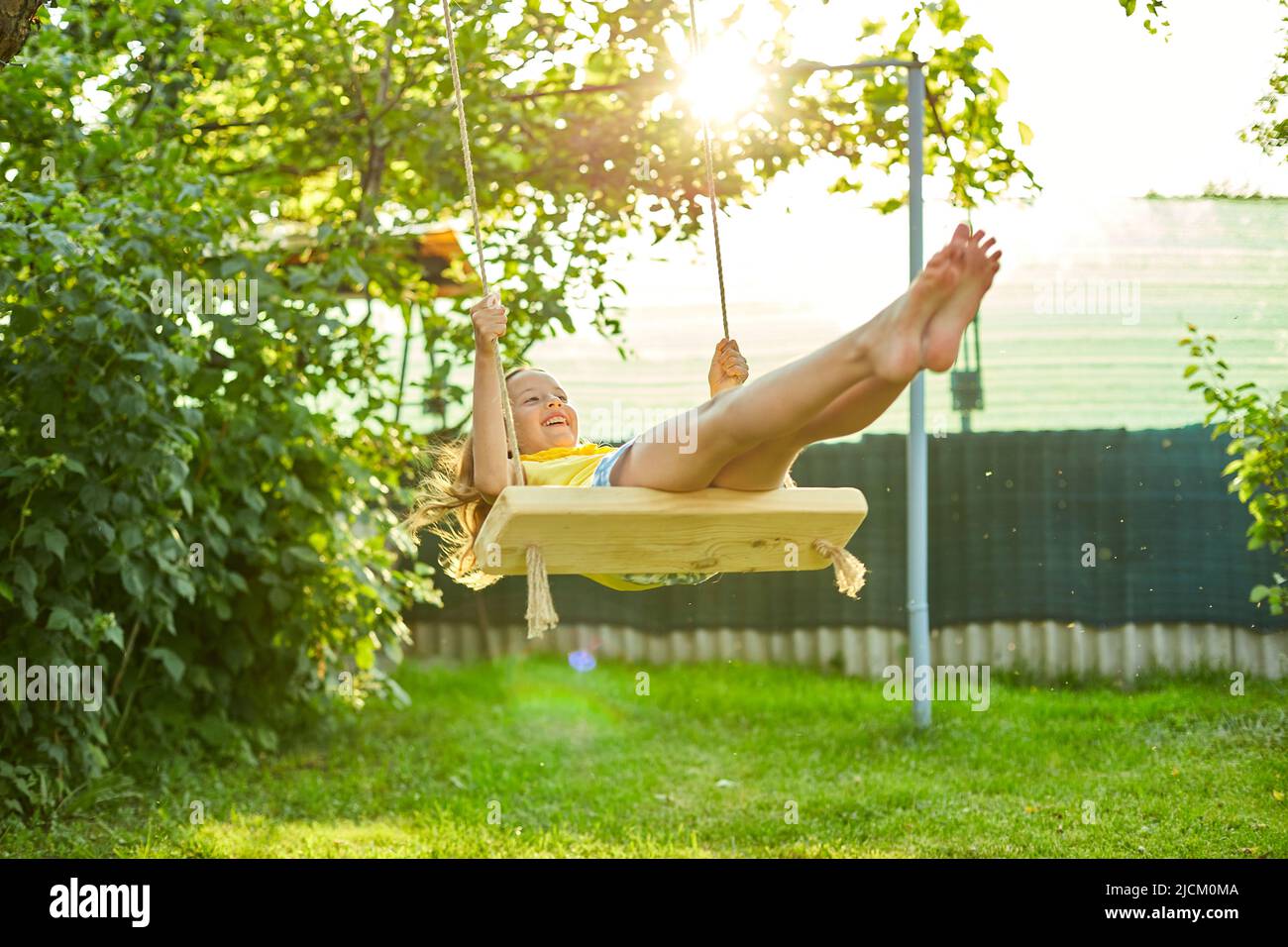 Happy barefoot laughing child girl swinging on a swing in sunset summer ...
