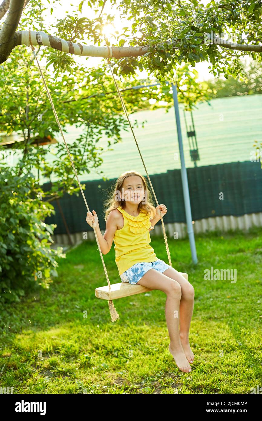 Happy barefoot laughing child girl swinging on a swing in sunset summer ...