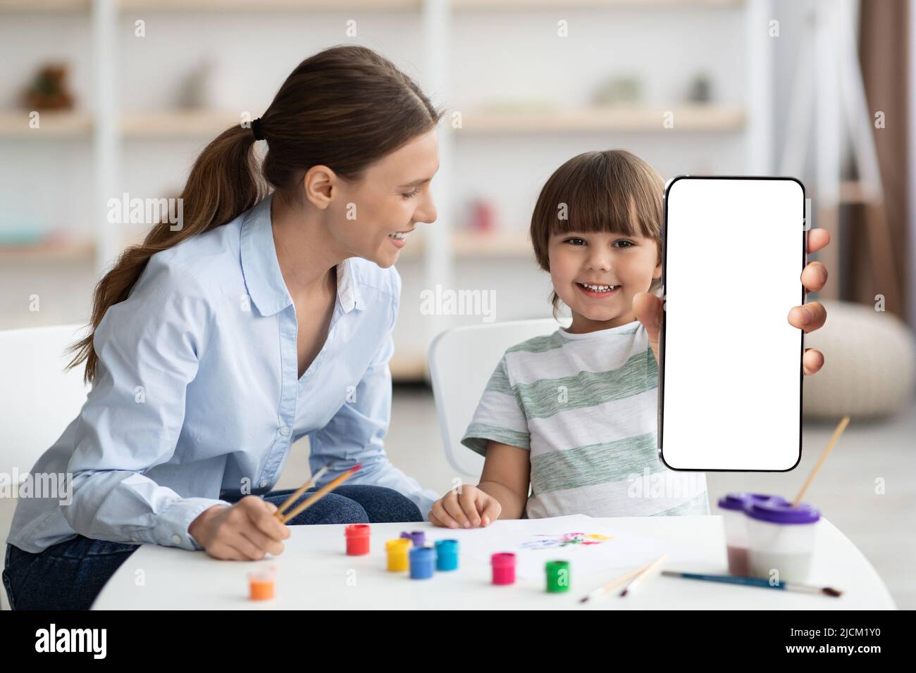 Little boy showing blank smartphone to camera during painting class ...