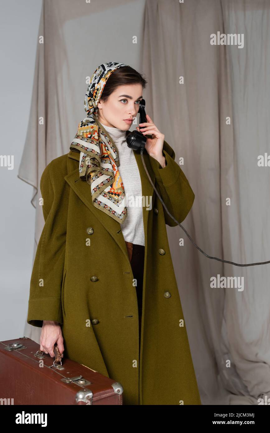 woman in green coat and patterned kerchief holding suitcase and talking ...