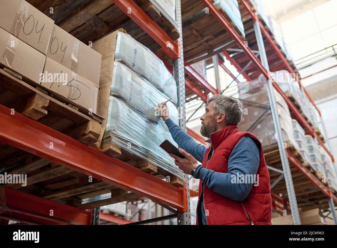 Mature worker using tablet pc and noting packages on shelves at ...