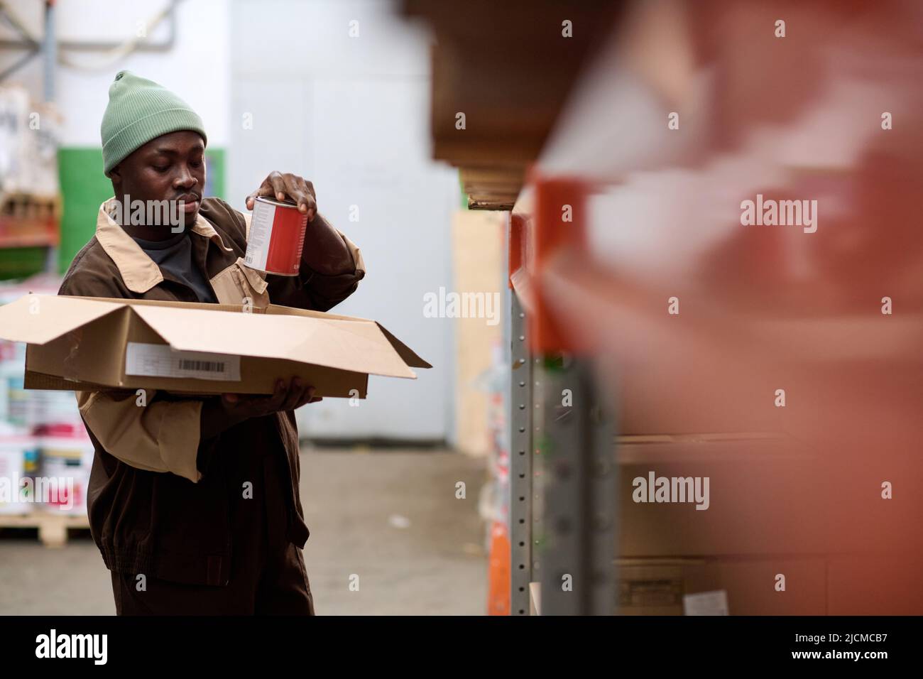 African American warehouse worker taking goods from shelves and packing ...