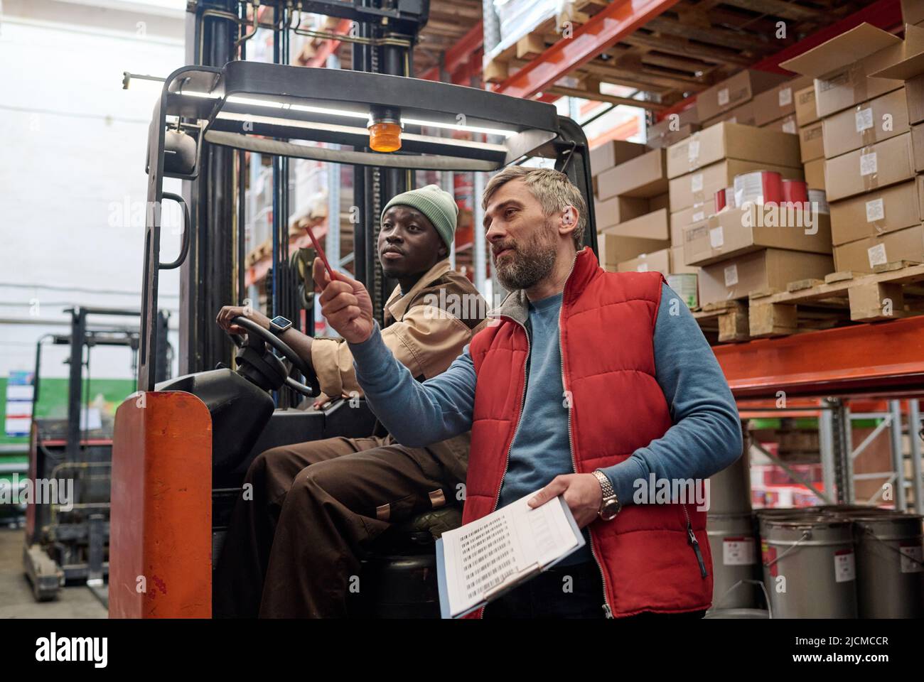 Manager with checklist giving instruction to forklift worker during ...