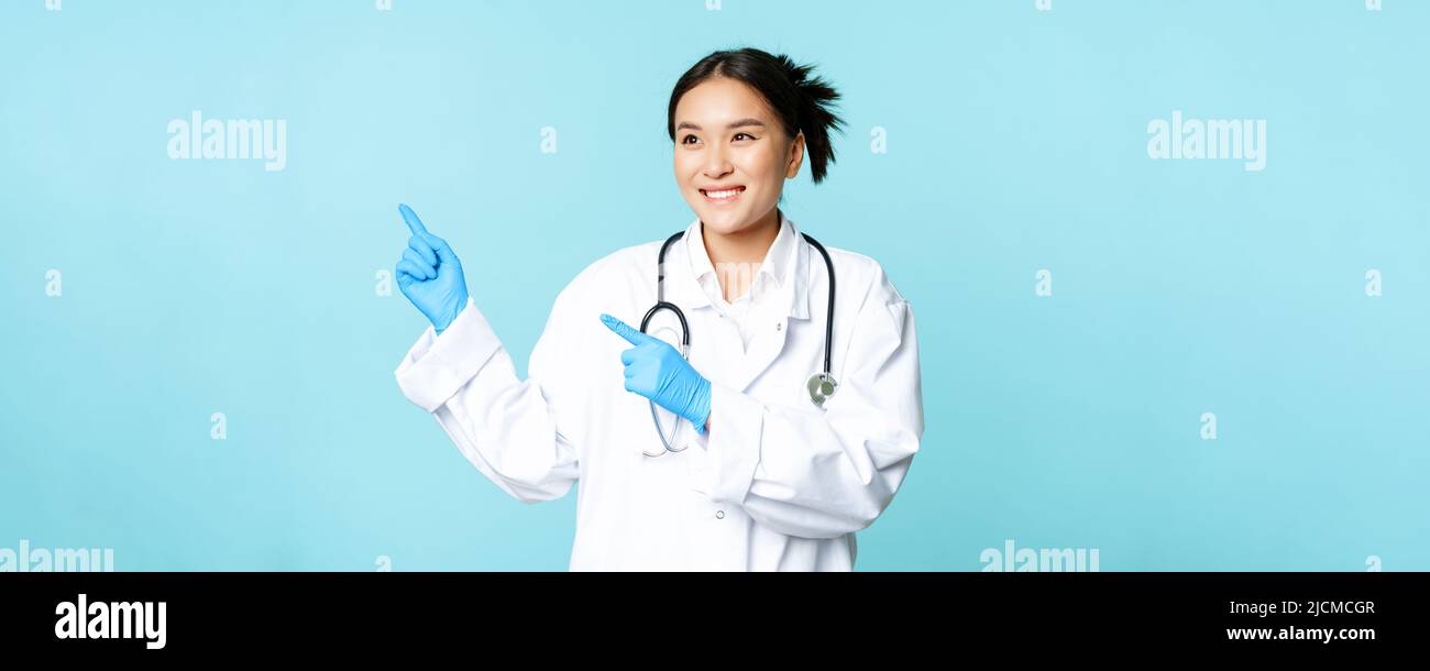 Asian smiling doctor, medical healthcare worker, pointing fingers left ...