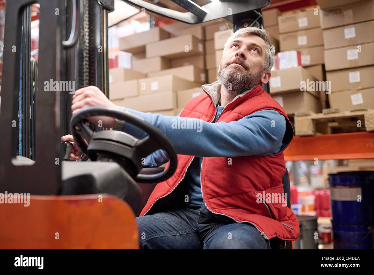 Mature warehouse worker looking on high shelves during loading cargo ...