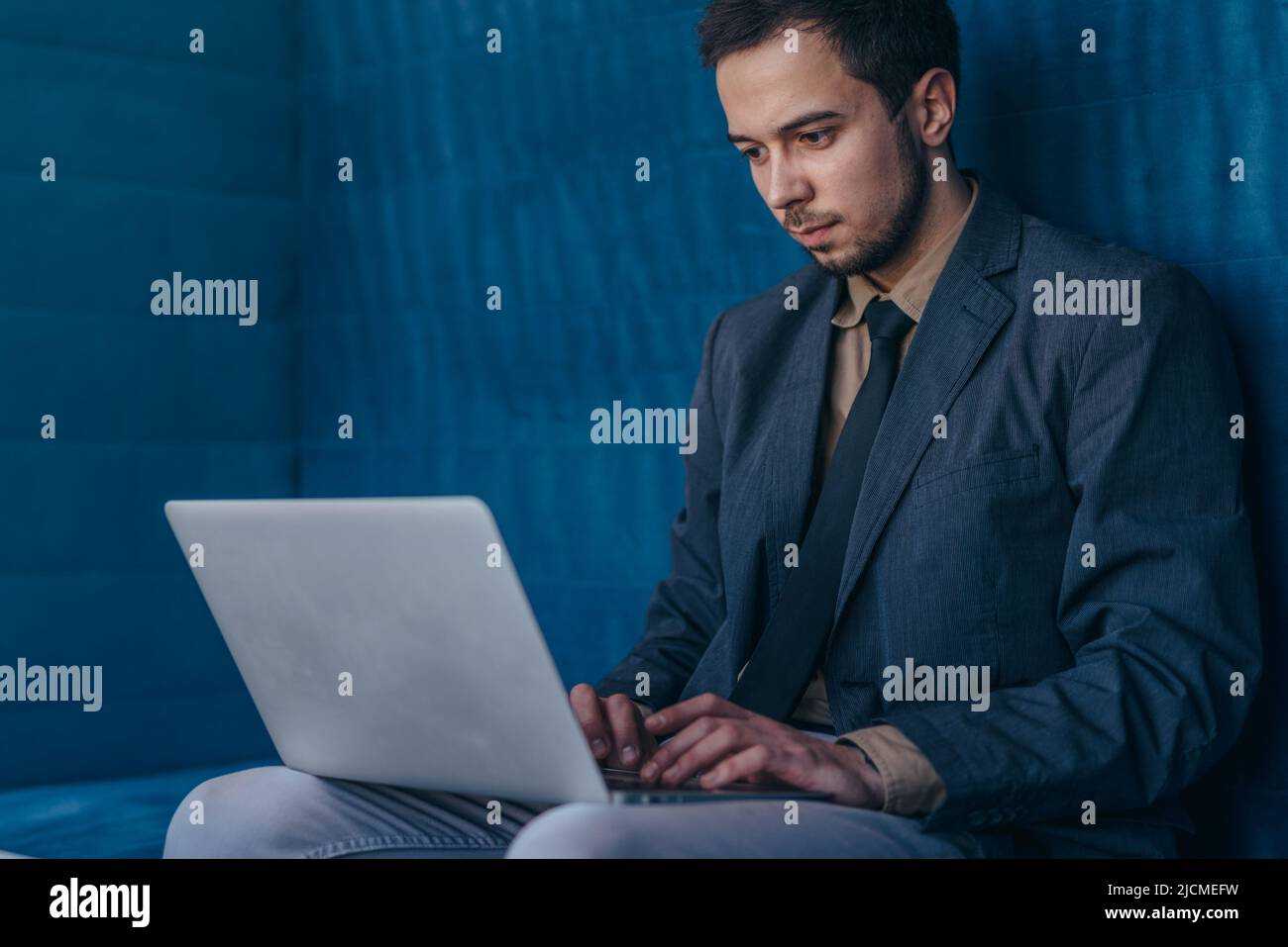 Portrait of young businessman working on laptop while sitting alone in ...